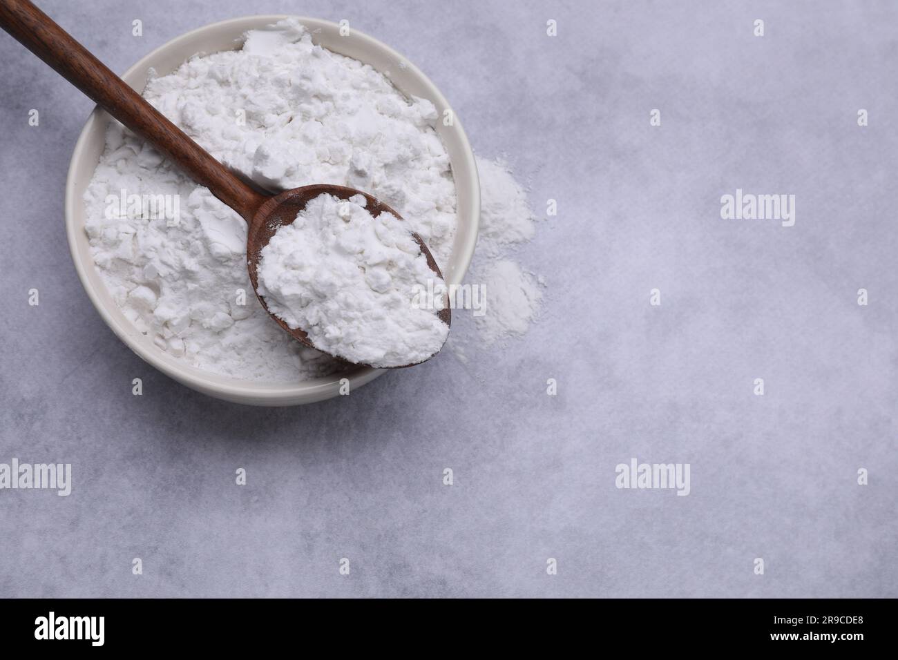 Spoon and bowl of starch on light gray table, top view. Space for text ...