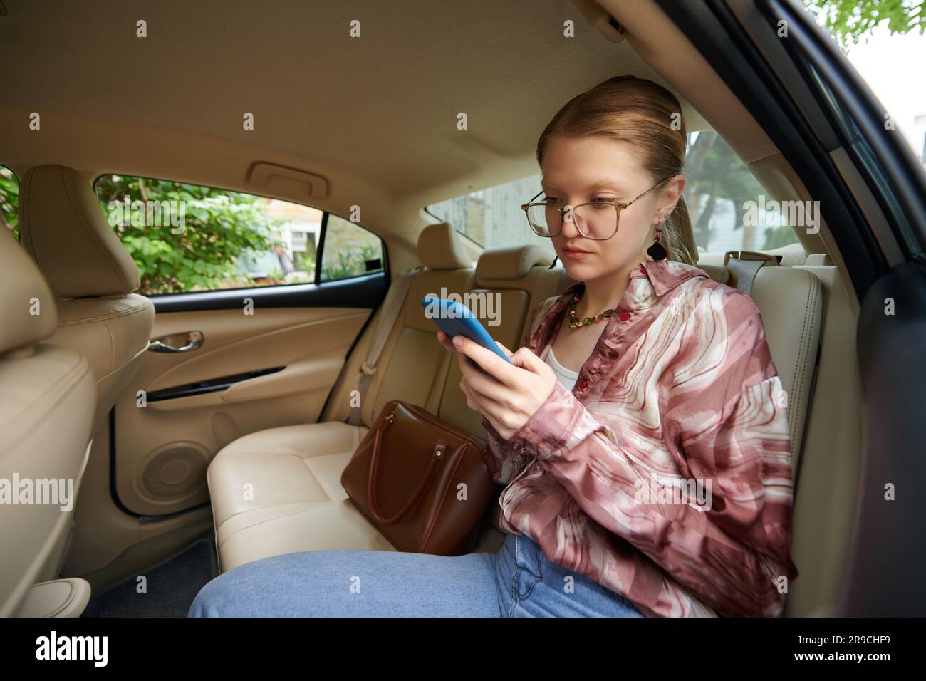 Serious young woman sitting on back seat of taxi car and texting ...