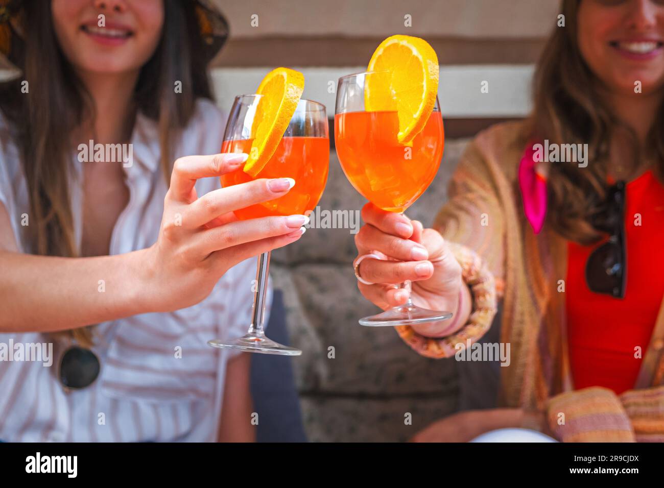 Two young women toast with spritz cocktails, extending their glasses ...