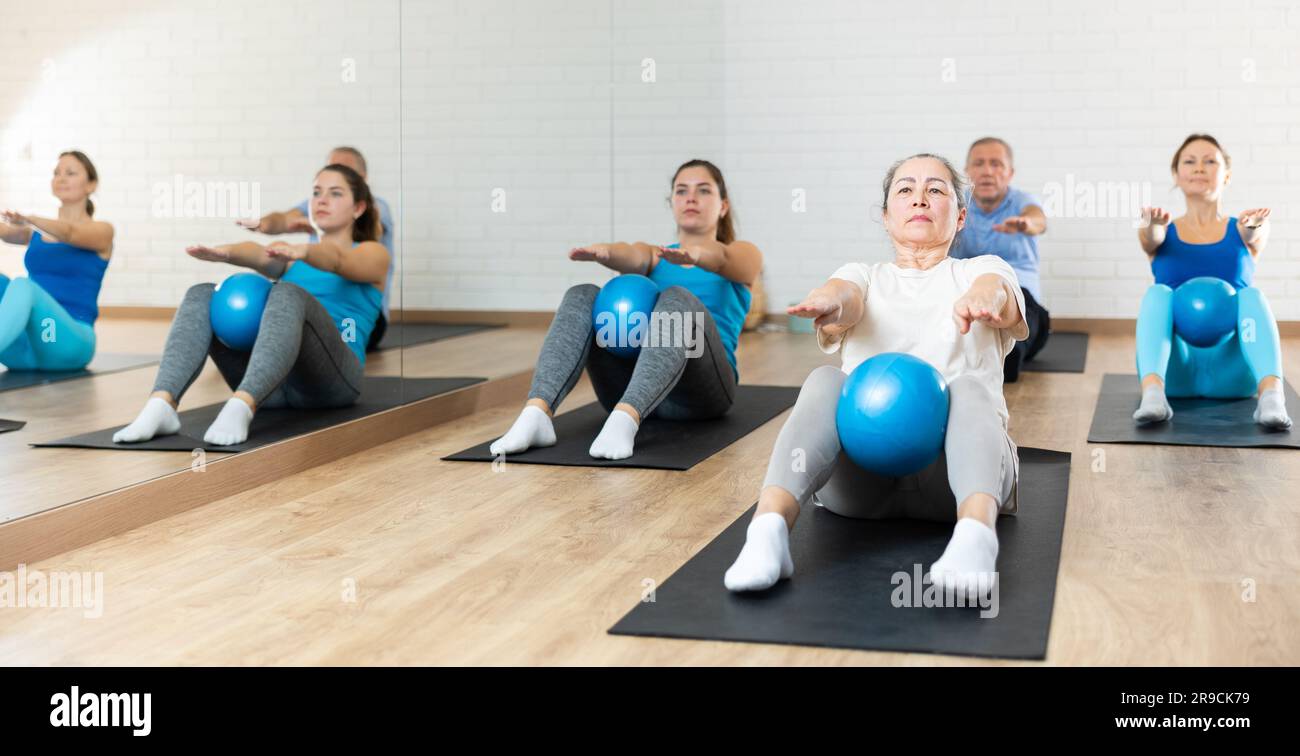 Aged woman sitting on mat and doing sit-ups with bender ball during ...