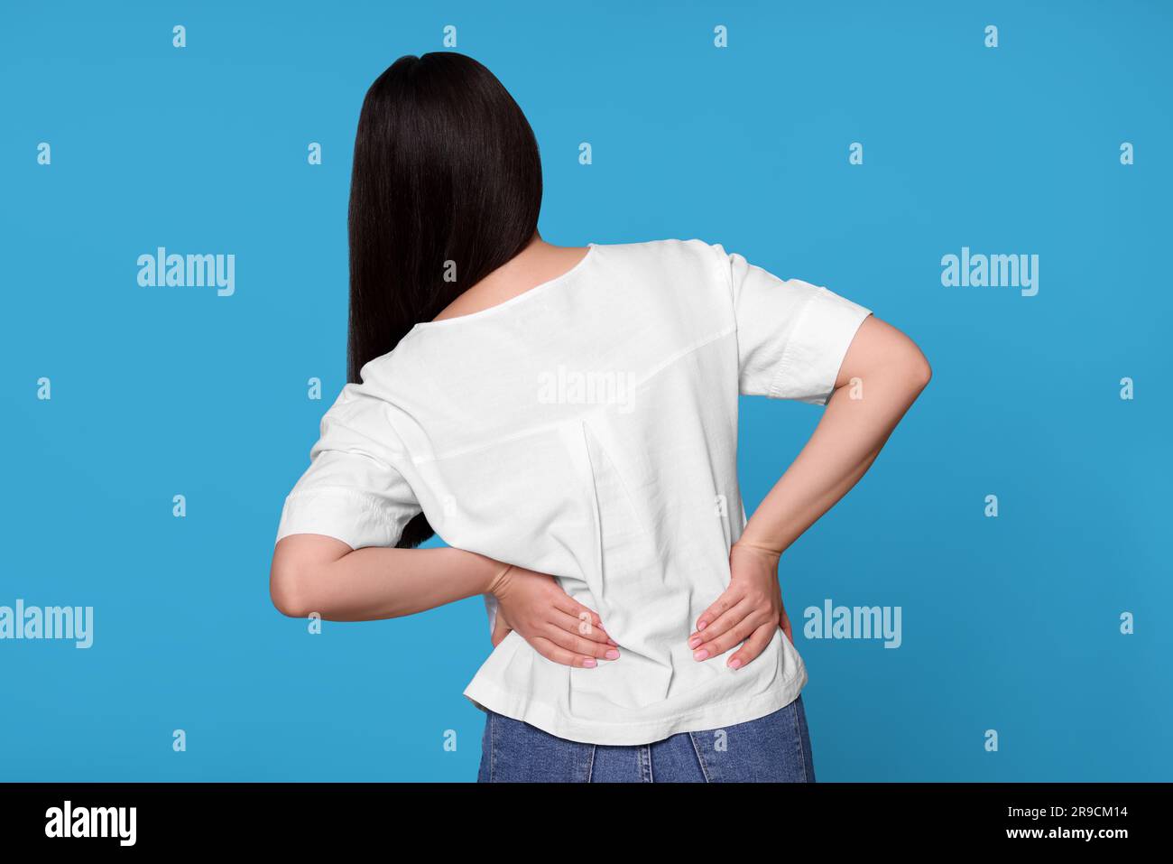 Young woman suffering from pain in back on light blue background ...