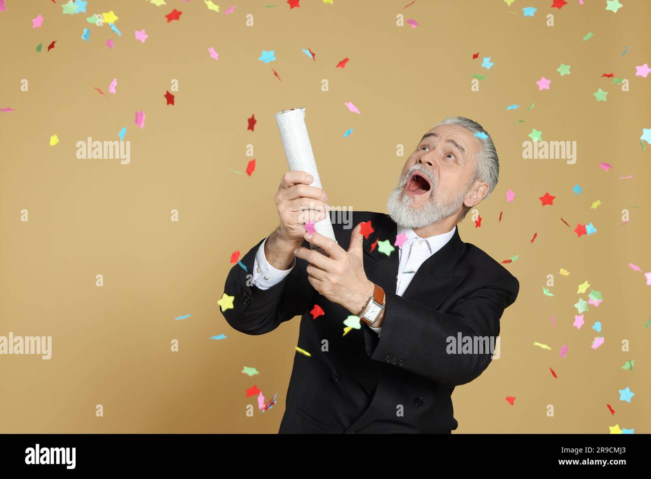 Emotional man blowing up party popper on beige background Stock Photo ...