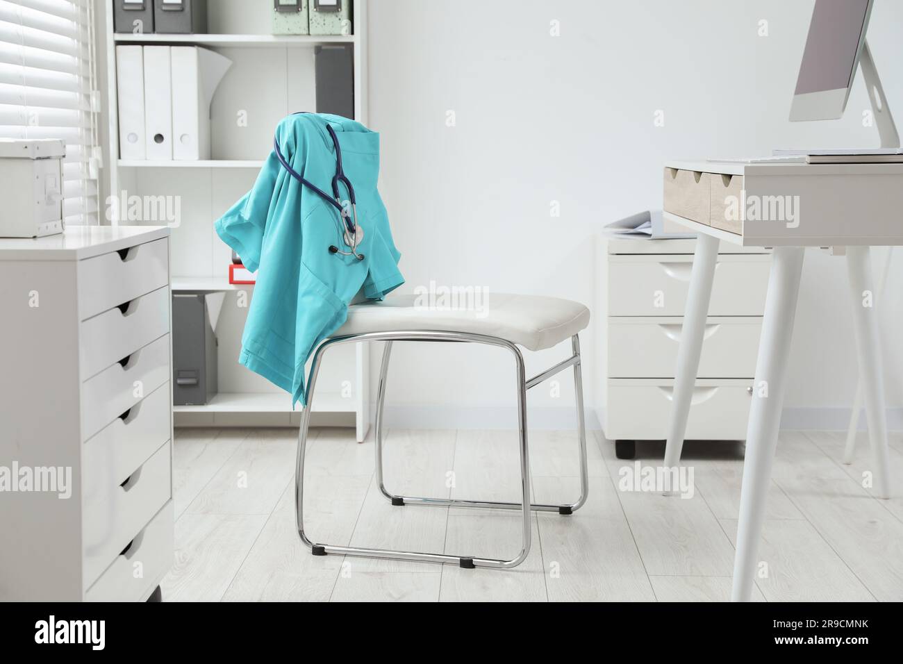 Turquoise medical uniform and stethoscope hanging on chair in clinic ...