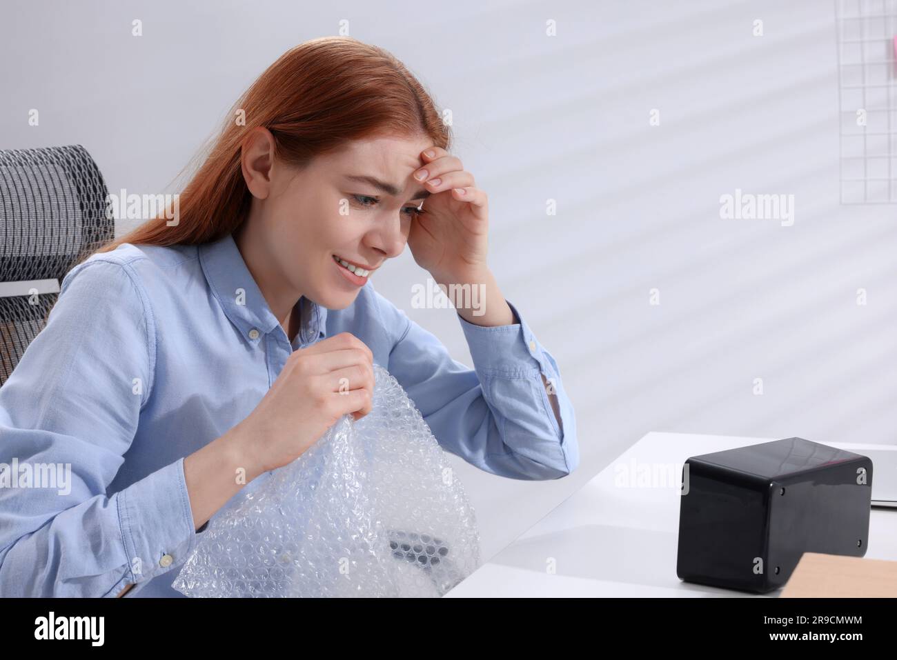 Emotional woman popping bubble wrap at desk in office. Stress relief ...