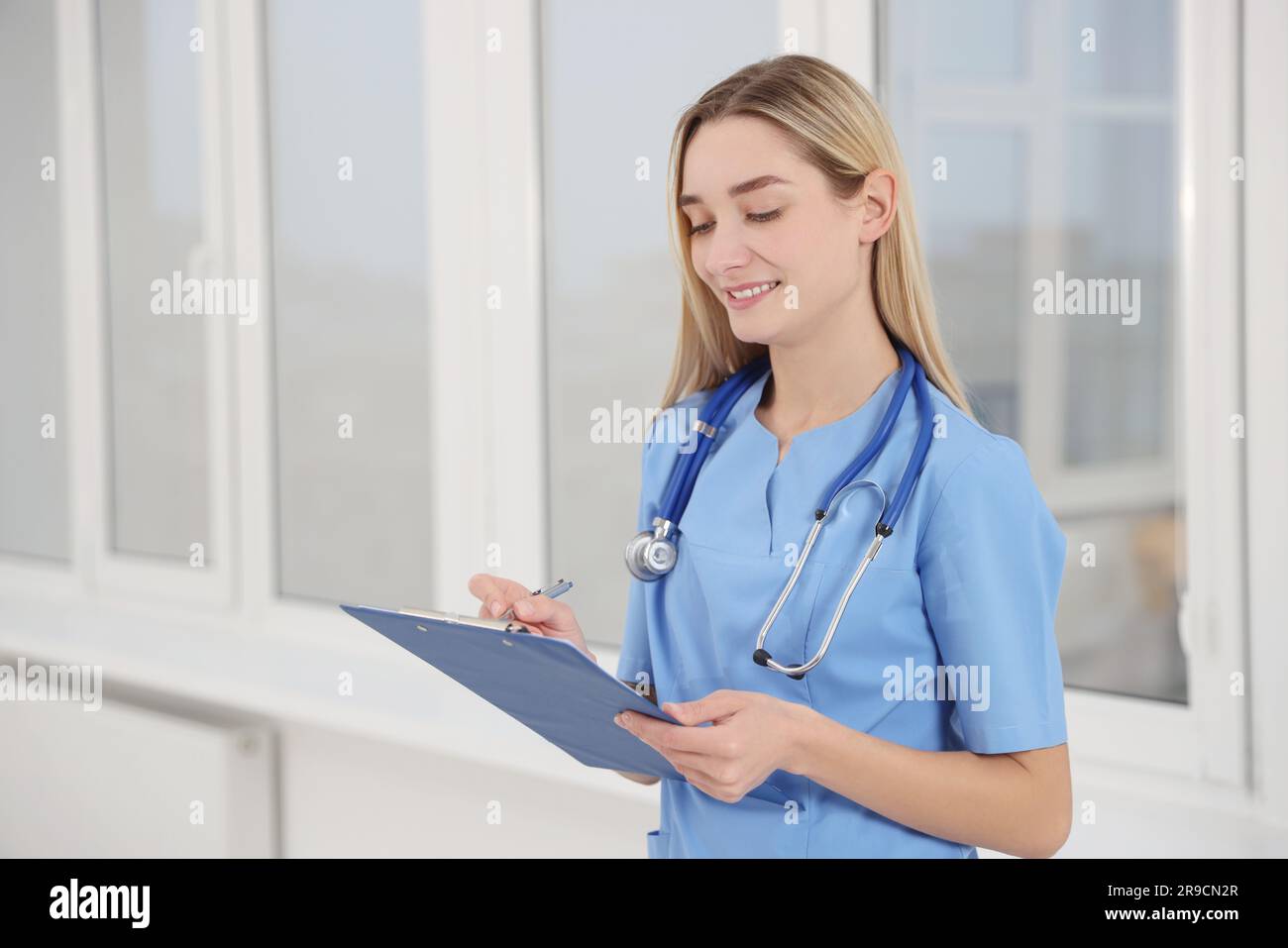 Young intern wearing uniform with clipboard in university hall, space ...