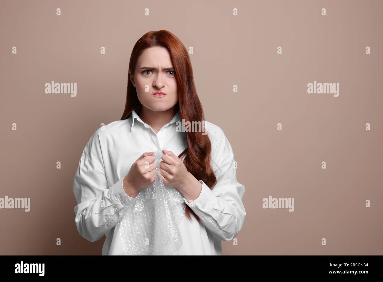 Angry woman popping bubble wrap on beige background. Stress relief ...