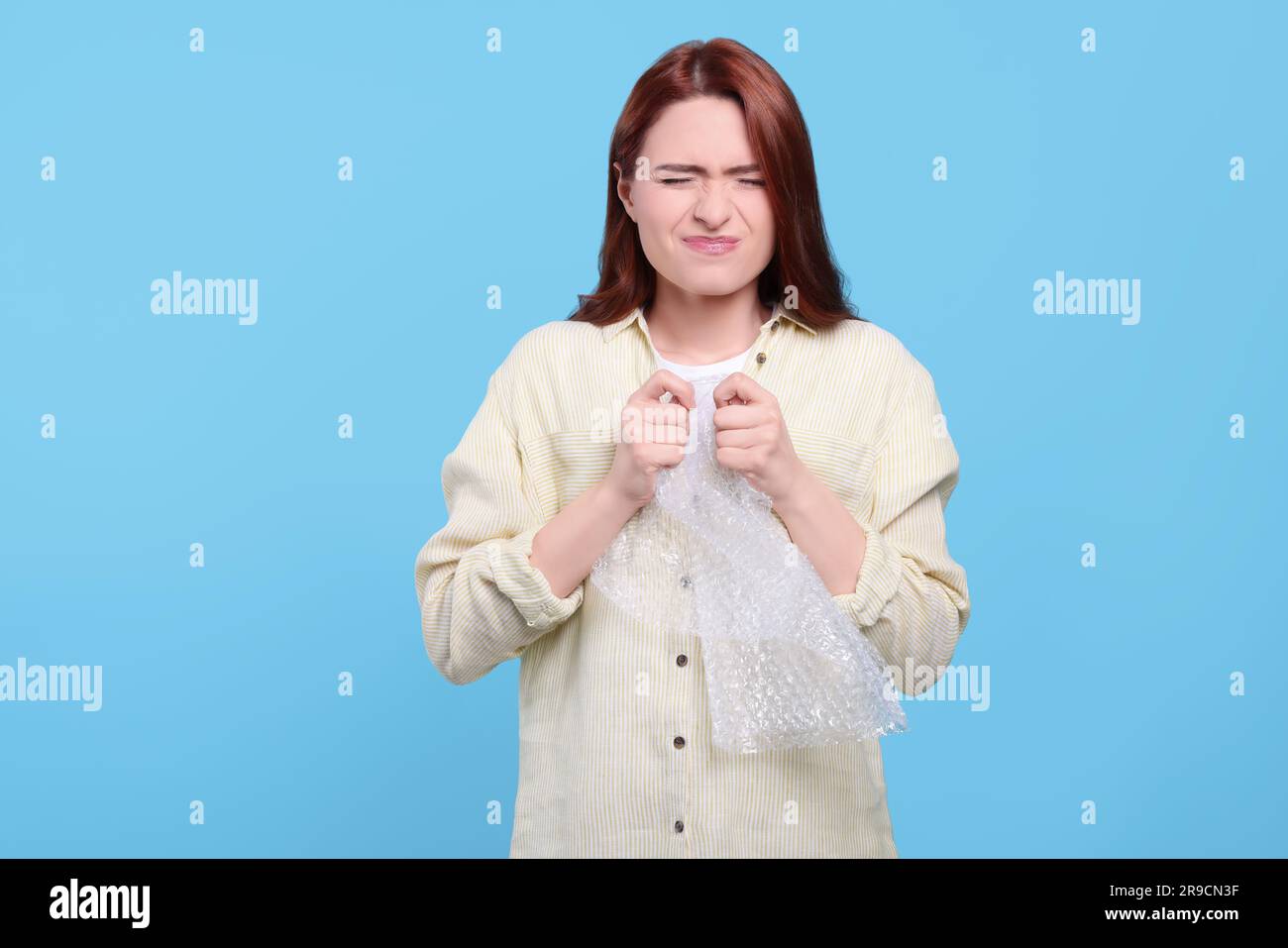Angry woman popping bubble wrap on turquoise background. Stress relief ...