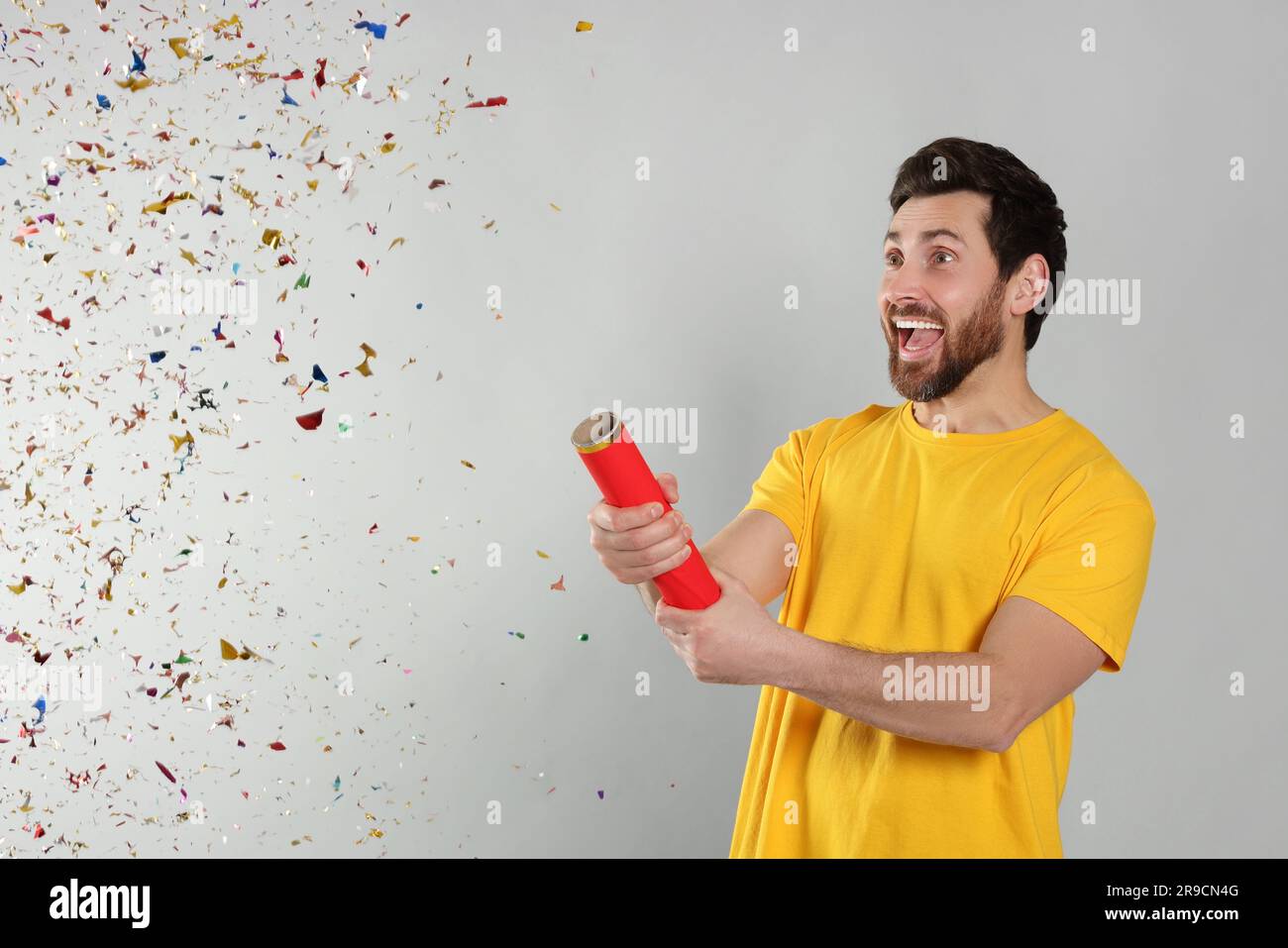 Emotional man blowing up party popper on light grey background Stock ...