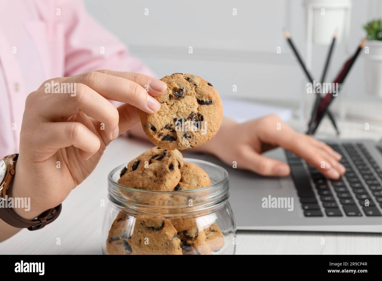 Office worker taking chocolate chip cookie from jar at workplace ...