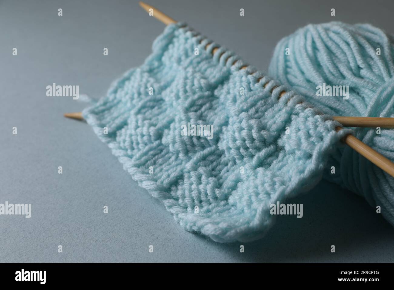 Soft turquoise knitting and needles on light blue background, closeup ...