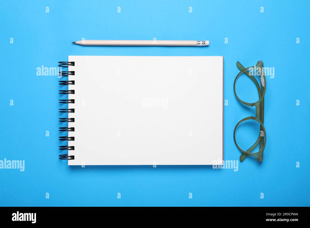 Open notebook, pencil and glasses on light blue background, flat lay ...