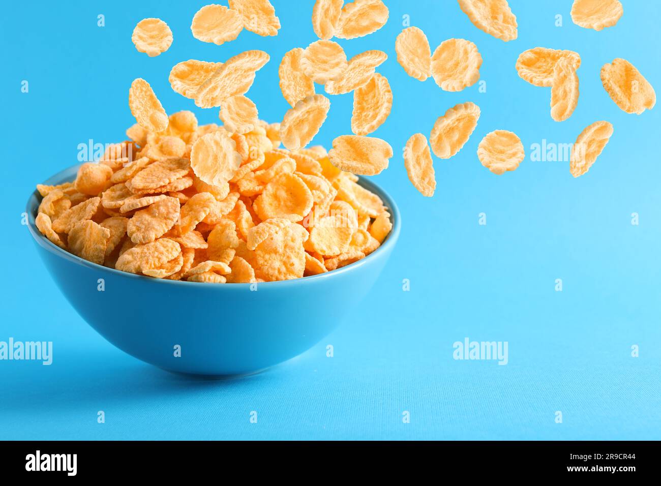 Tasty corn flakes falling into bowl on light blue background Stock ...