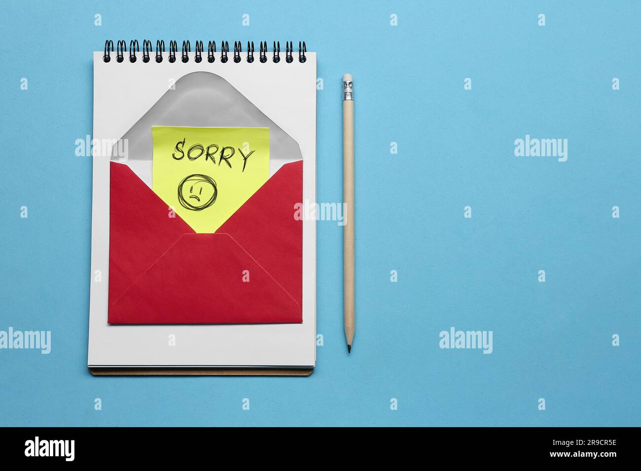 Note with word Sorry and drawn sad face in envelope, notebook and ...