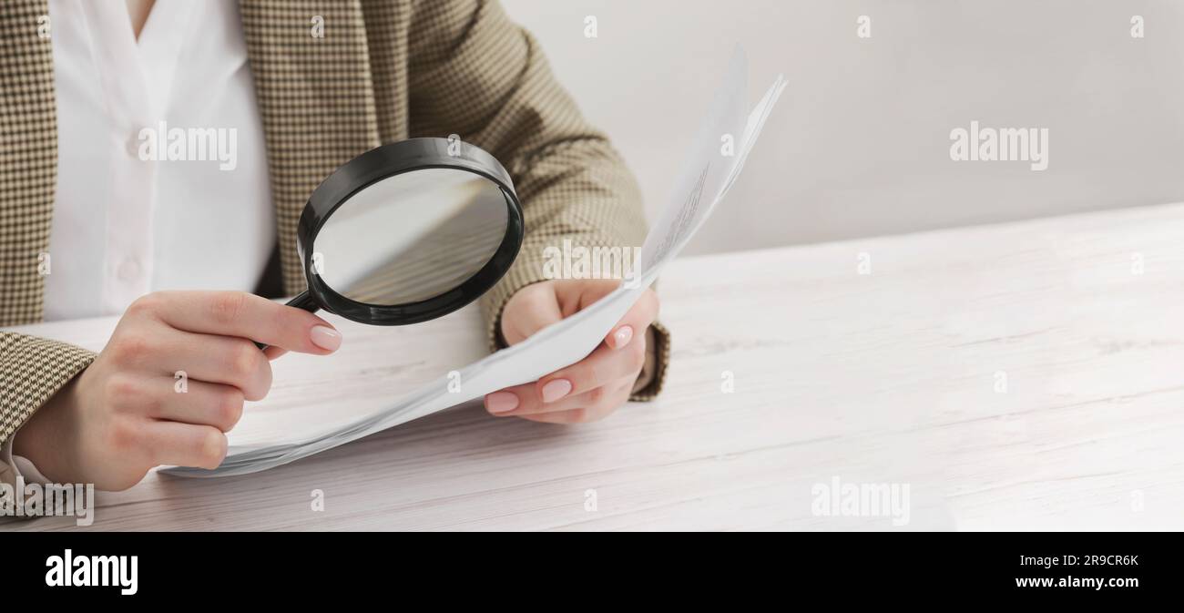 Woman looking at documents through magnifier at white wooden table ...