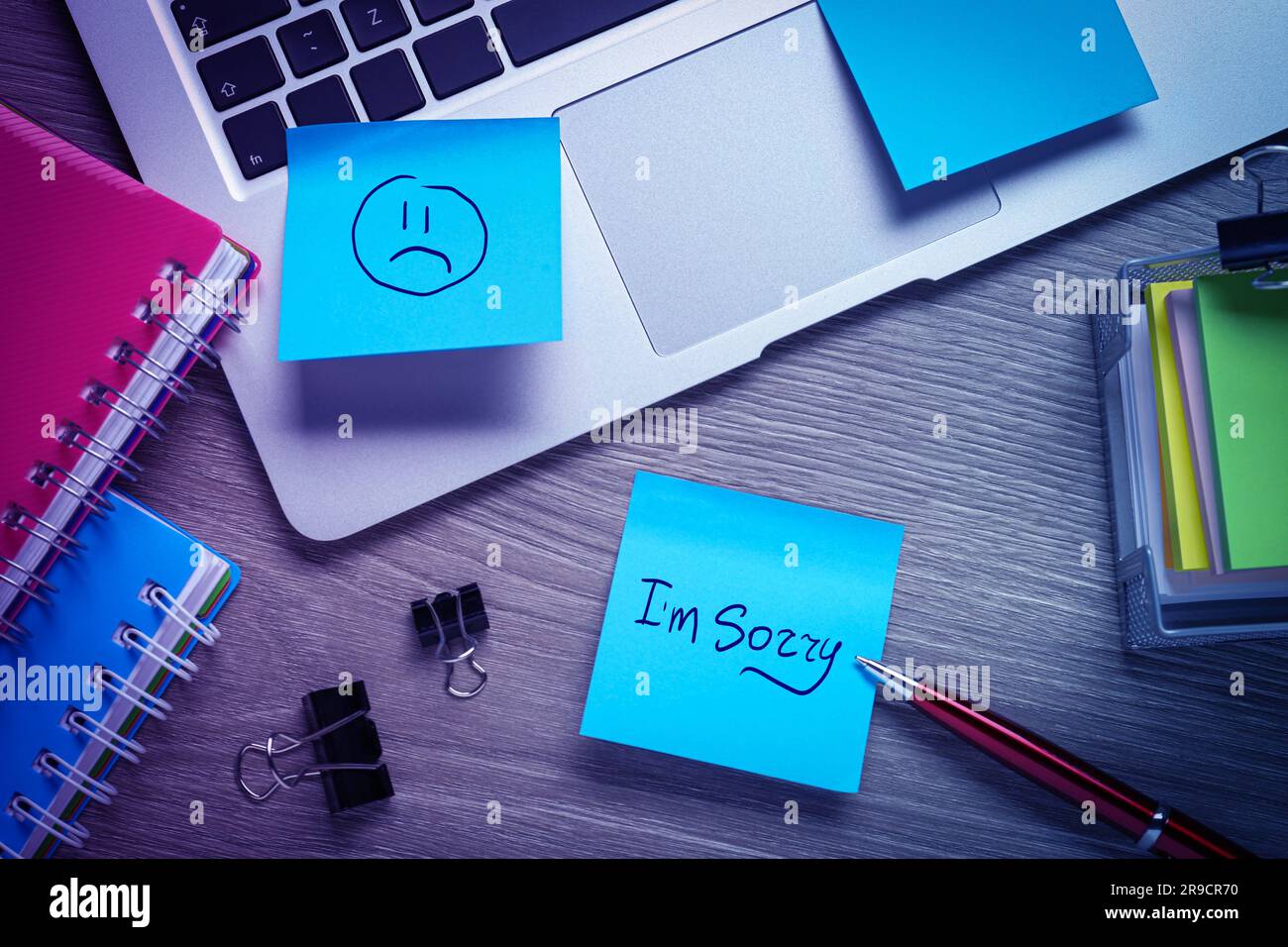 Sticky notes with word Sorry and drawn sad face on workplace. Laptop ...