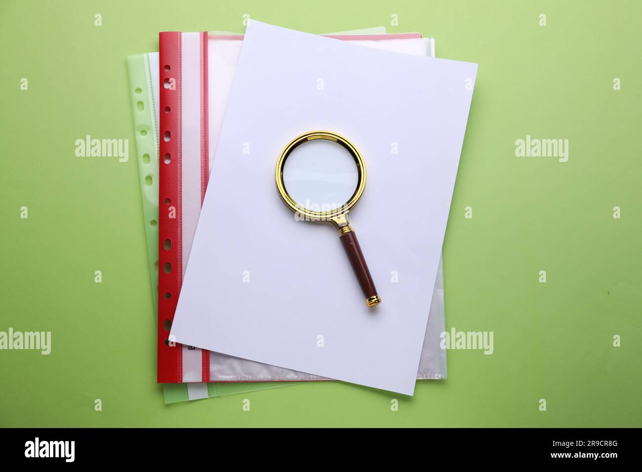Magnifying glass and folders with paper sheets on light green ...