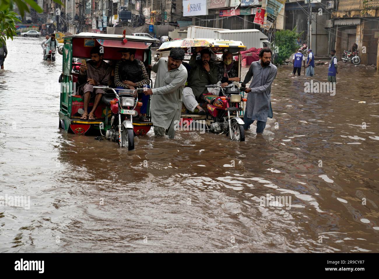 Drivers push their motorcycle rickshaws through a flooded road caused ...