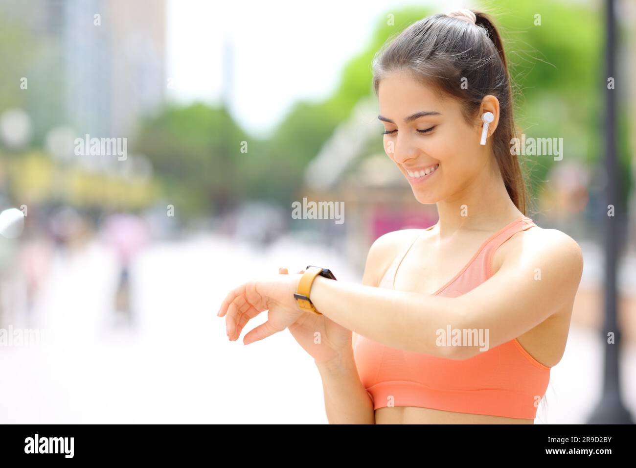 Happy runner wearing earbud selecting music on smartwatch before run in ...