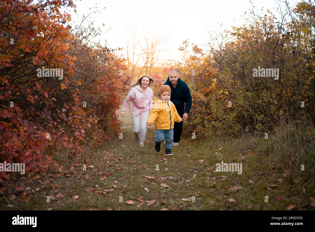 Beautiful young family on a walk in autumn forest. Parents running for little son. Happy family ...