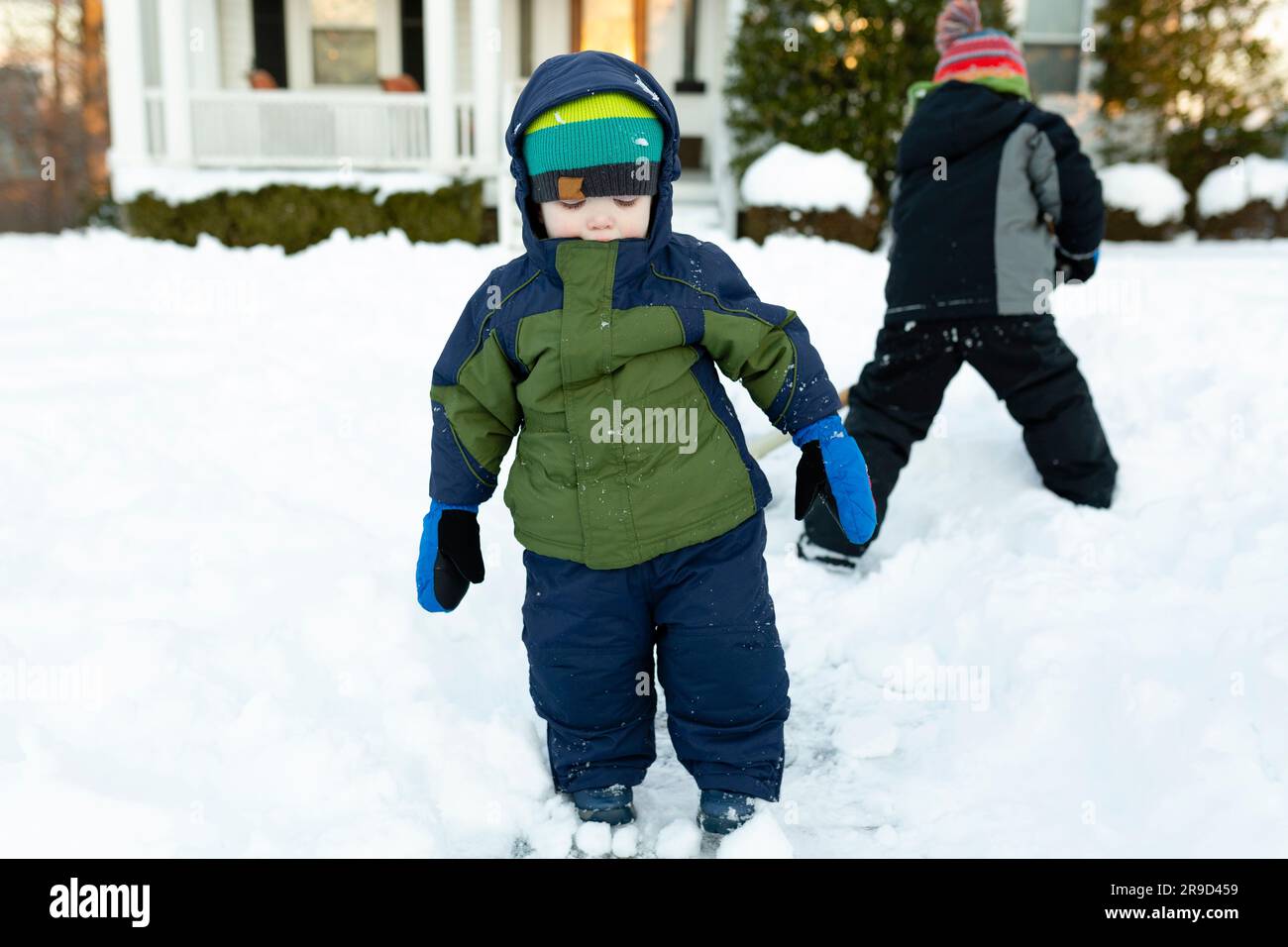 Two boys stand in snow in front yard during winter wearing winter gear ...