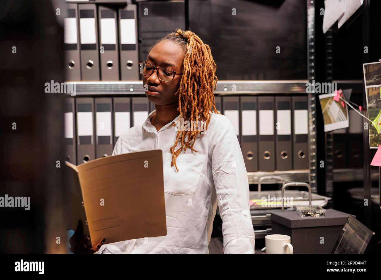 Policewoman standing near crime case folders shelf and reading report ...