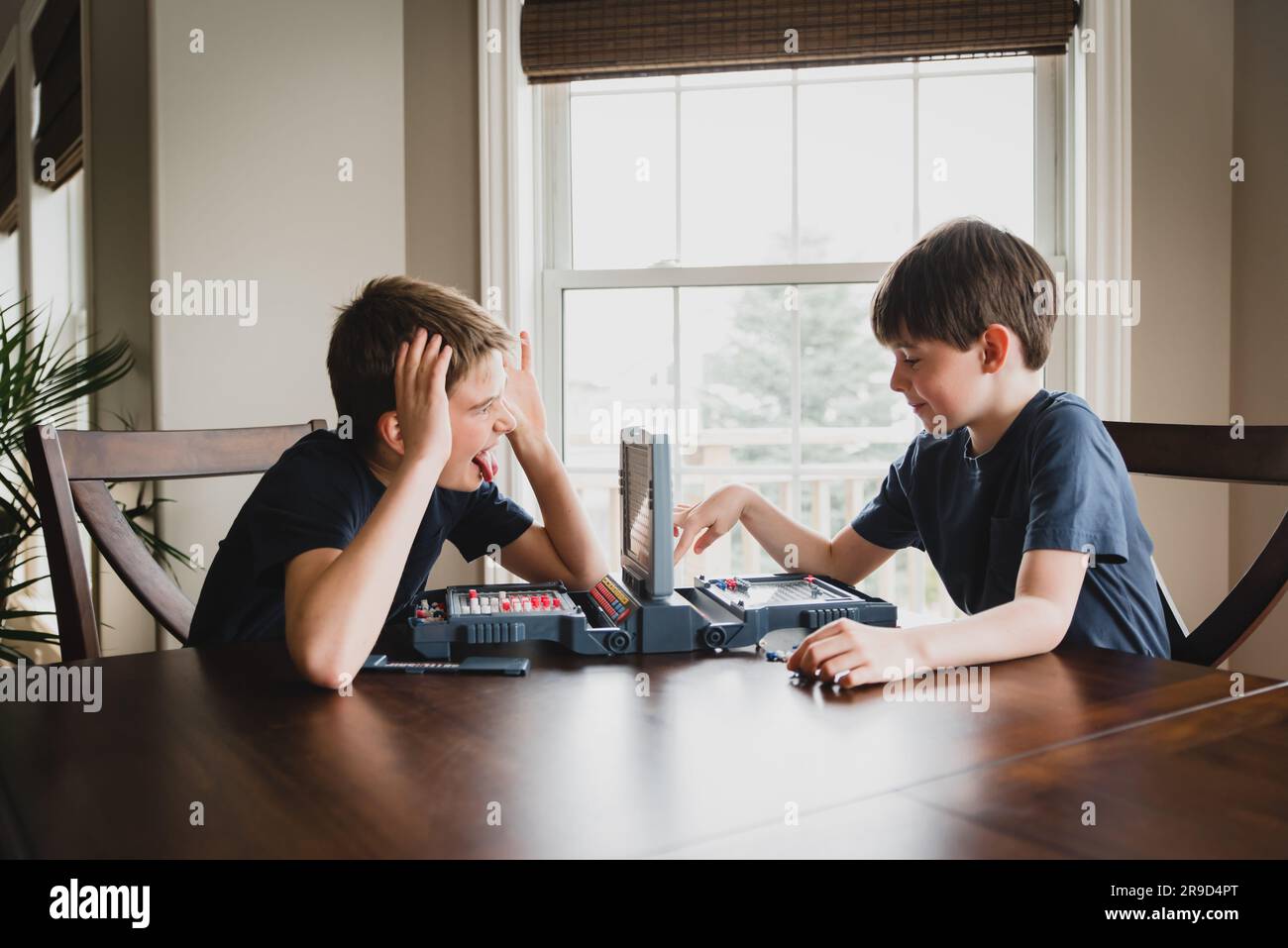 Boy making faces at his brother as they play a board game together ...