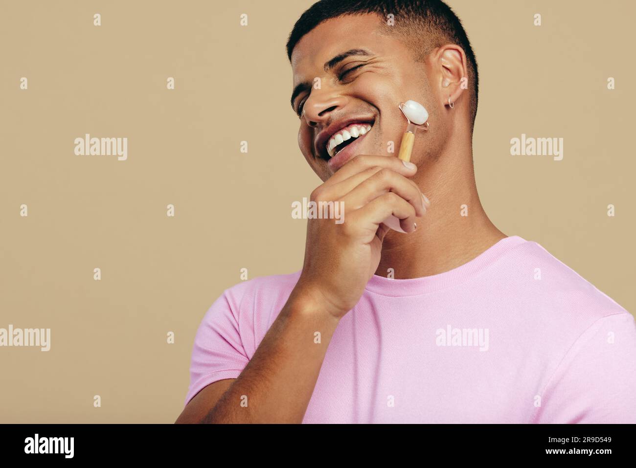 Man smiling as he lets a jade roller do its magic on his face in a grooming and self-care ...