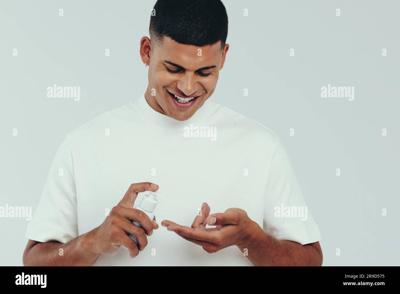 Happy young man putting facial wash on his fingers, preparing to apply the beauty product on his ...