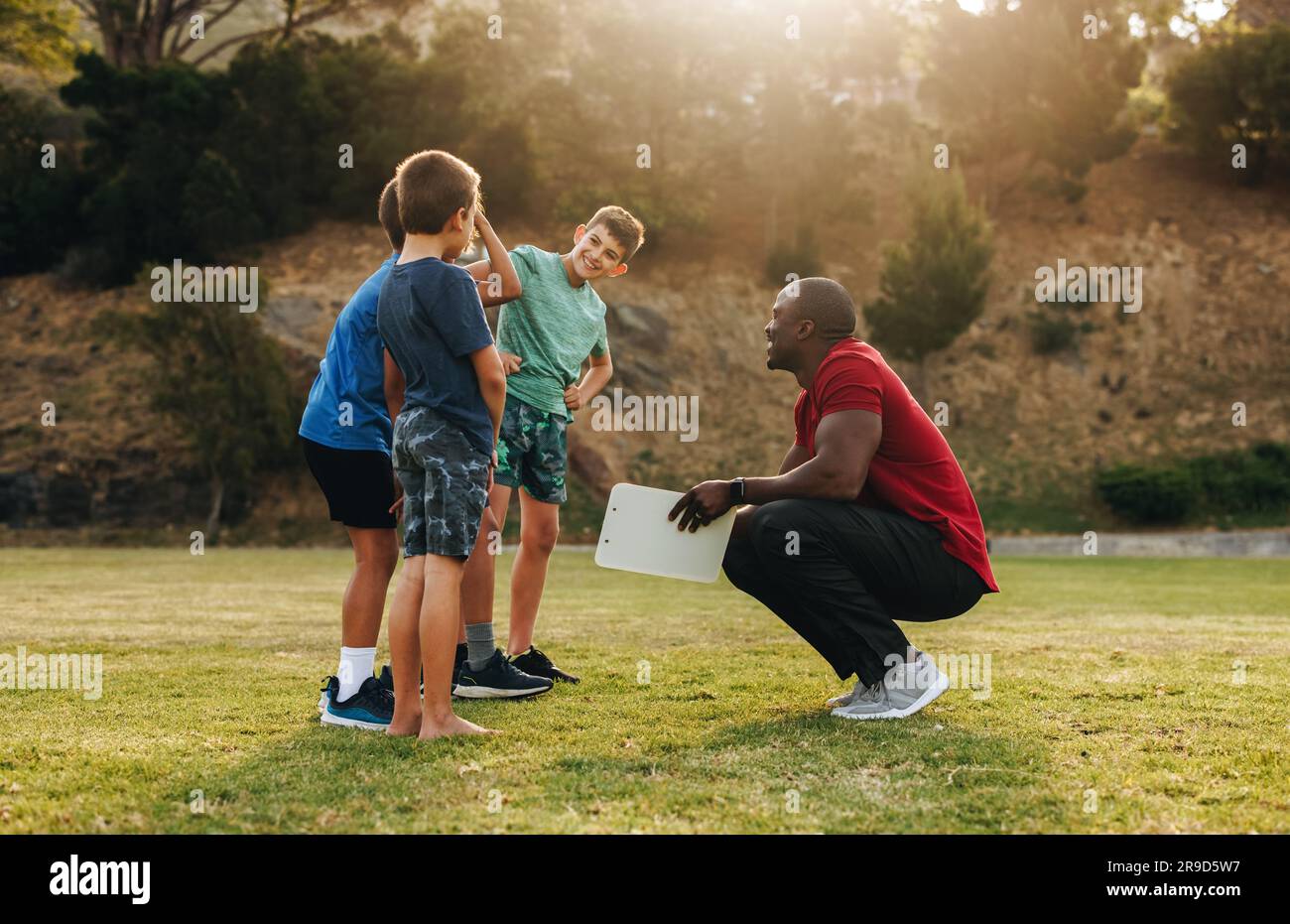 Coach having a team talk with a group of children in a school ground ...