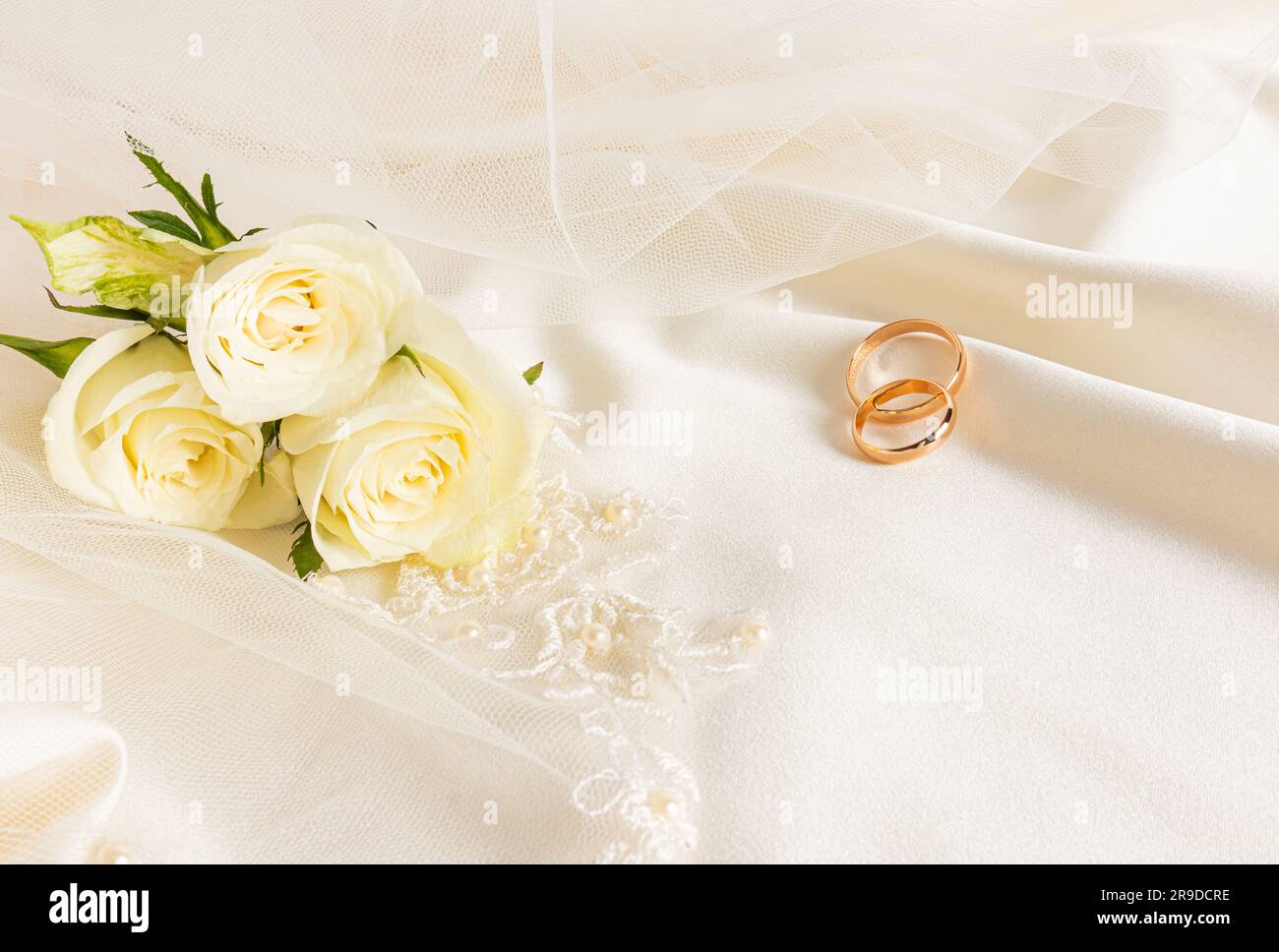 Two gold wedding rings leaned on the folds of satin beige fabric with a ...