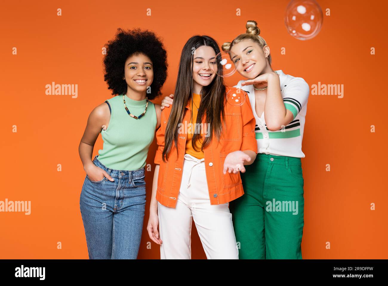 Joyful and multiethnic teen girlfriends in trendy casual outfits posing ...