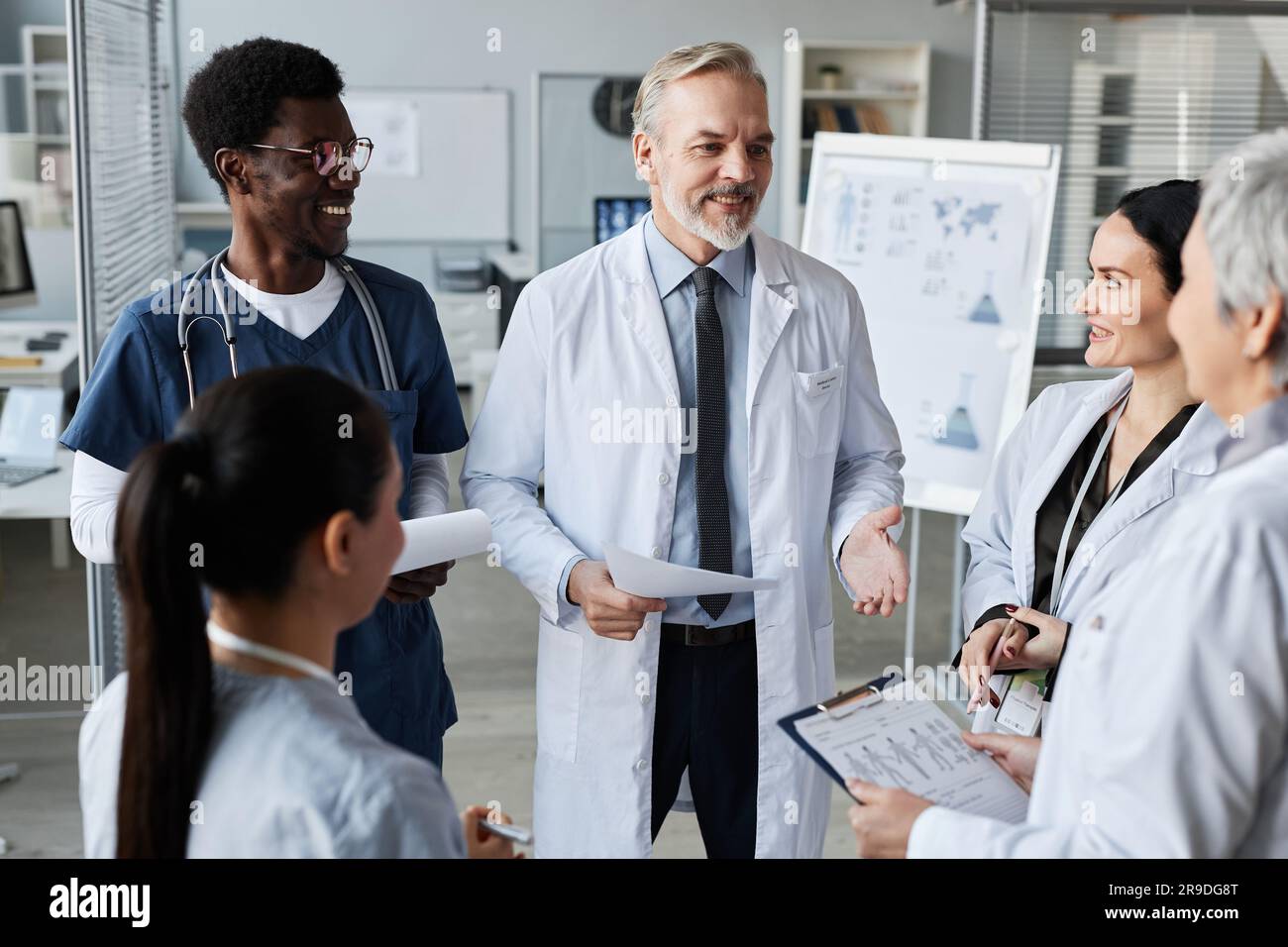 Smiling mature doctor in lab coat answering questions of young ...