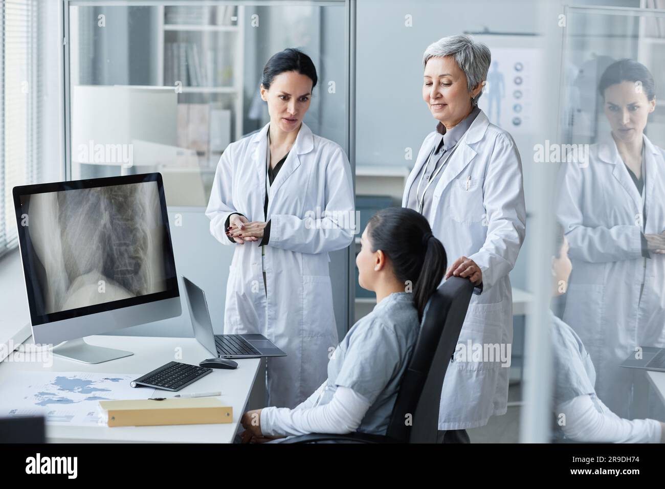 Group of three female radiologists in lab coats consulting about x-ray ...