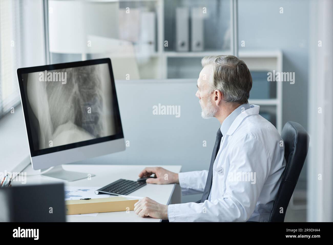 Mature male radiologist in lab coat looking at computer screen with x ...