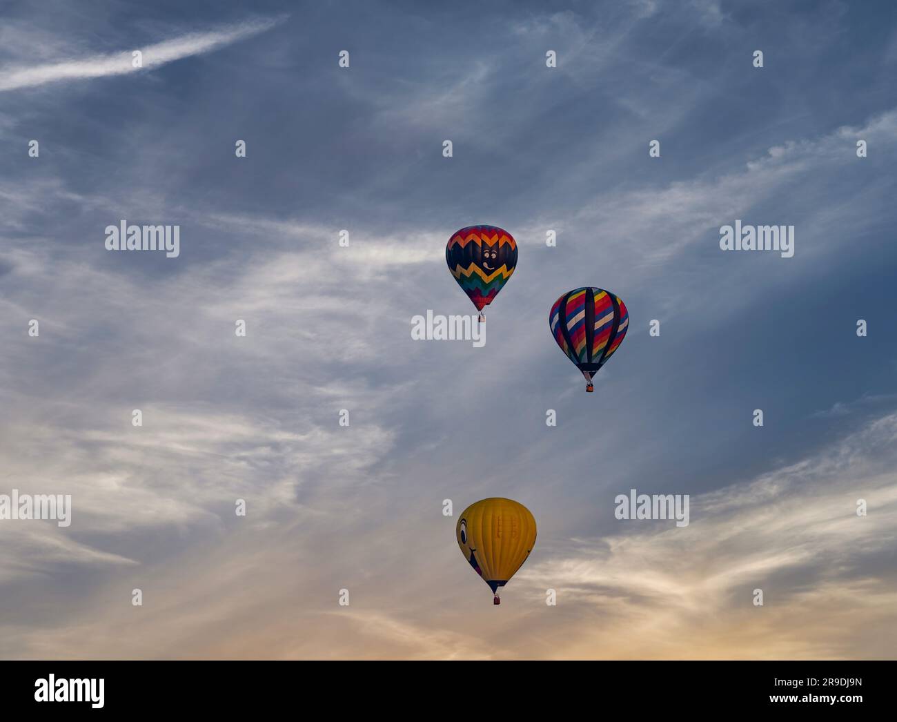 A view of multiple multi-colored hot air balloons floating in a blue sky with thin clouds Stock ...