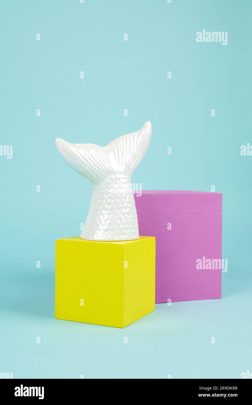 a mermaid tail in iridescent ceramic on a stack of pink and yellow ...