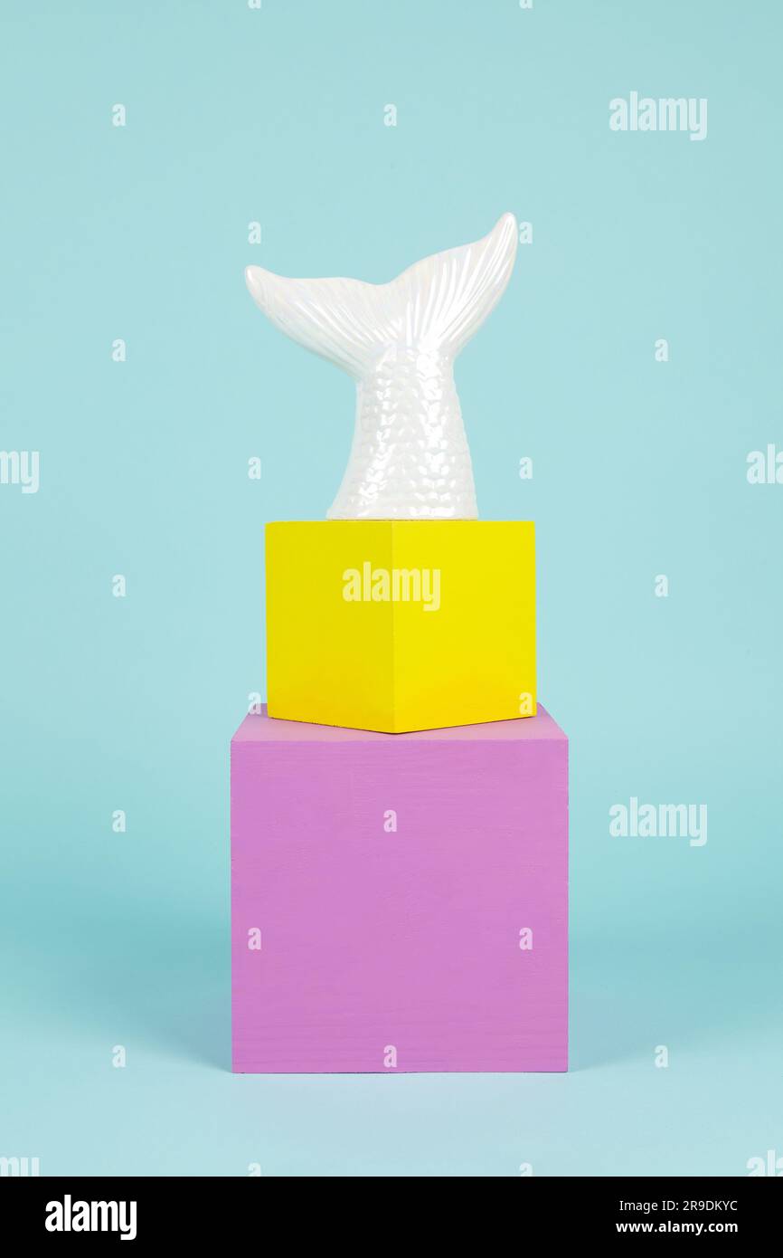 a mermaid tail in iridescent ceramic on a stack of pink and yellow ...