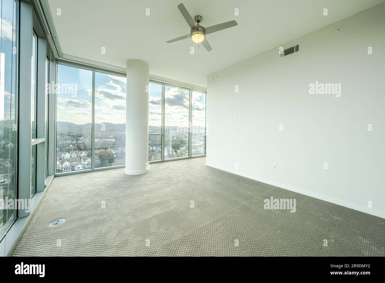 An airy and spacious interior with a ceiling fan and large windows ...