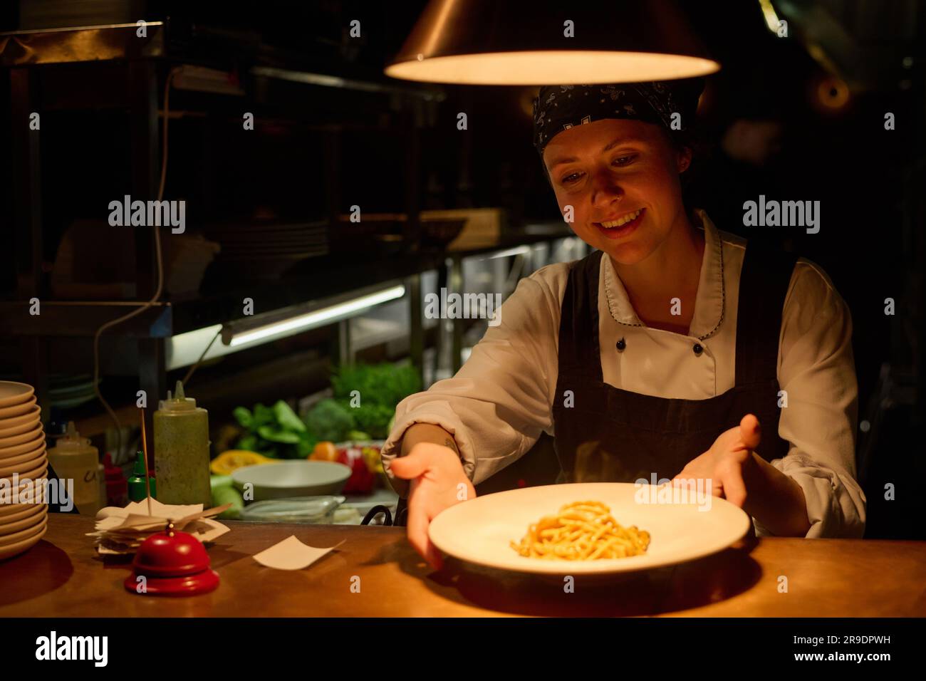 Happy young female worker of cafe in uniform putting plate with ...