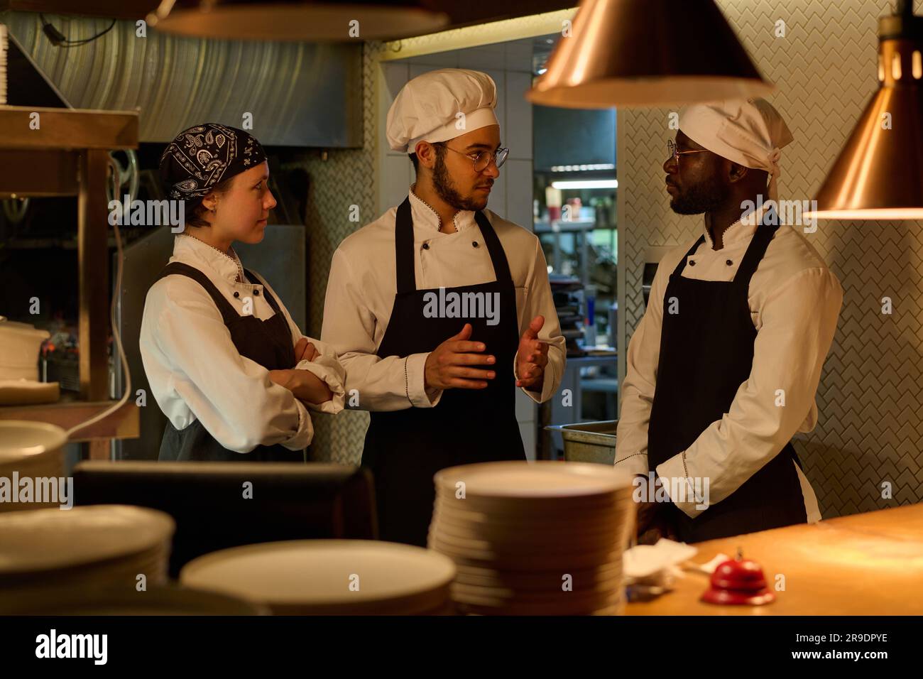 Three young intercultural cooks in uniform discussing working points in ...