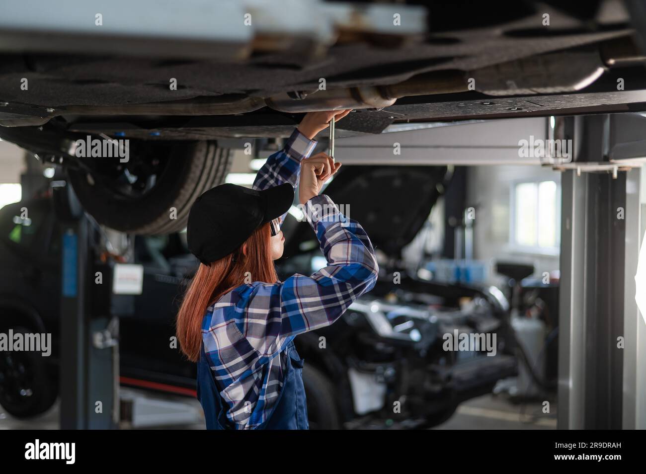 Female mechanic unscrew the nuts on the bottom of the car that is on ...