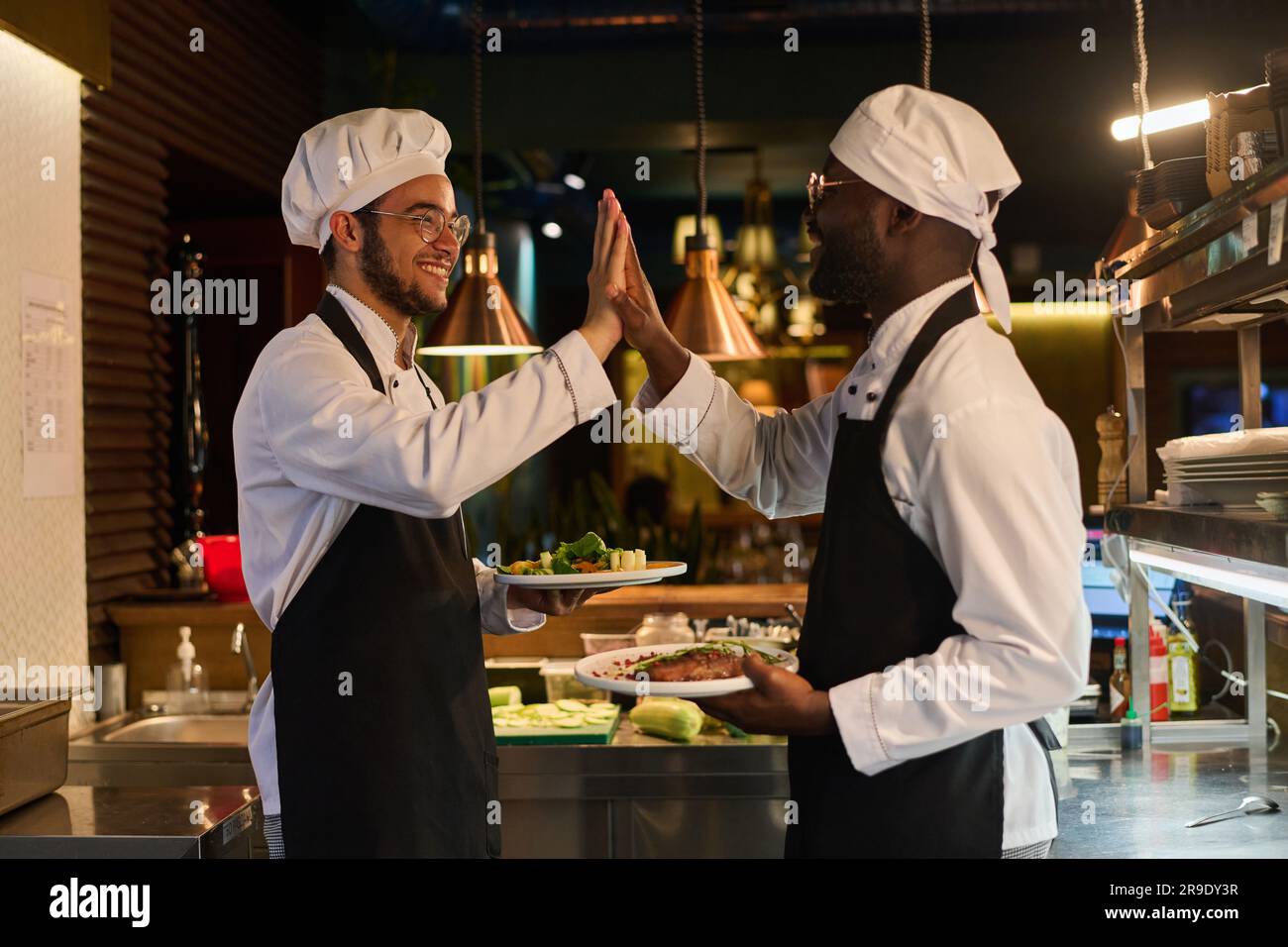 Side view of two happy young intercultural male waiters or cooks in ...
