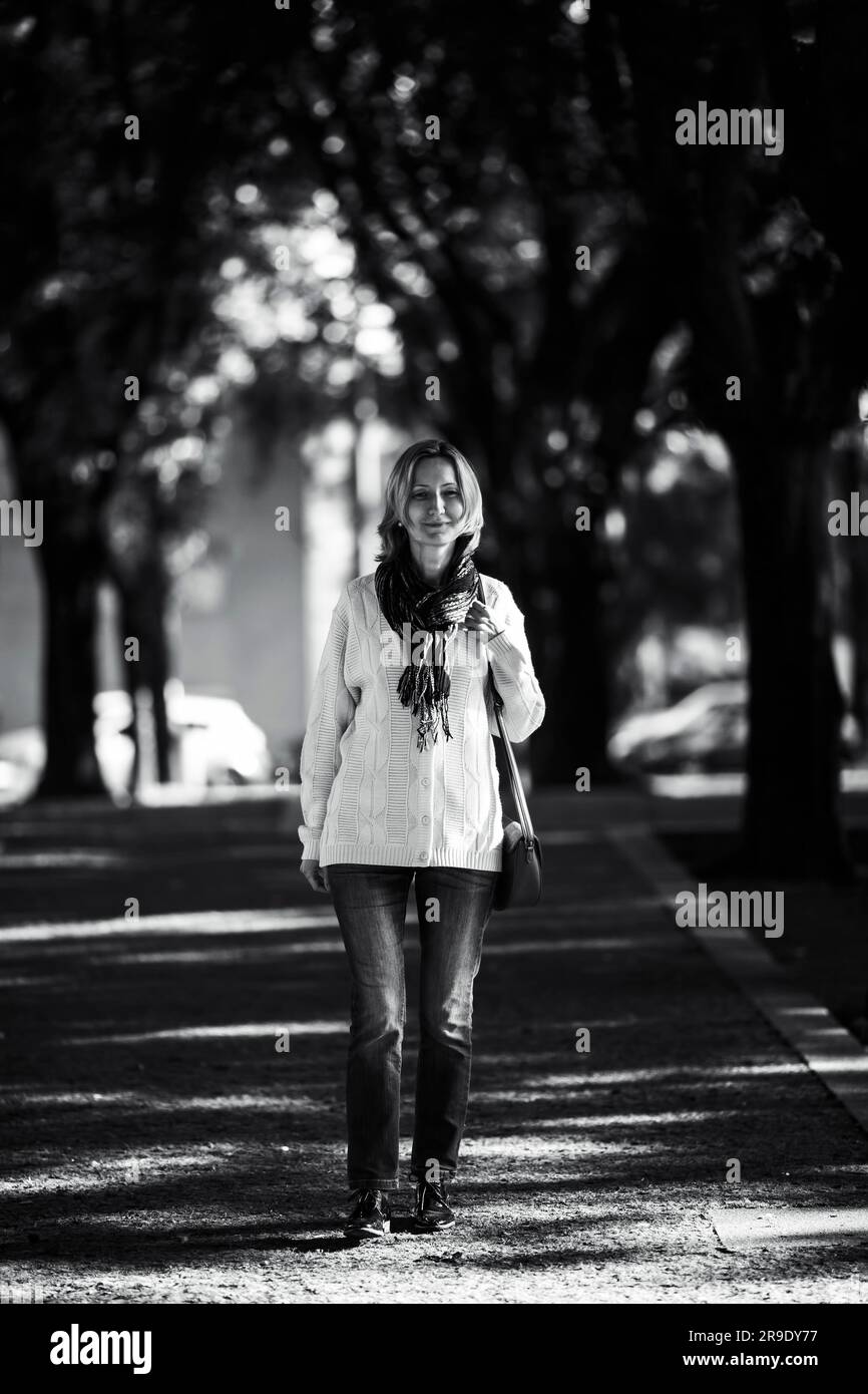 A woman is walking along an alleyway in a park. Black and white photo ...