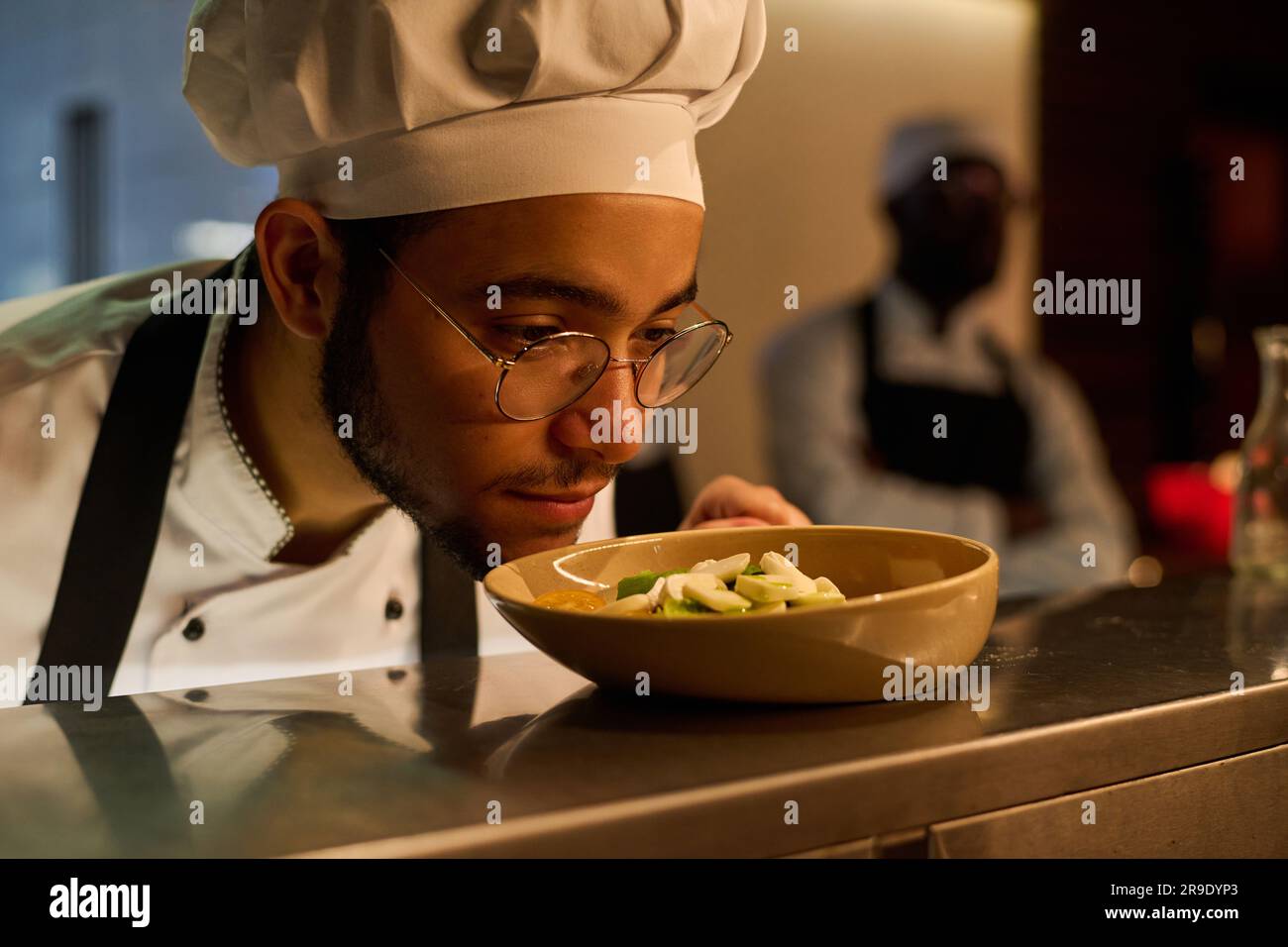 Face of young chef in uniform enjoying smell of fresh vegetarian salad ...