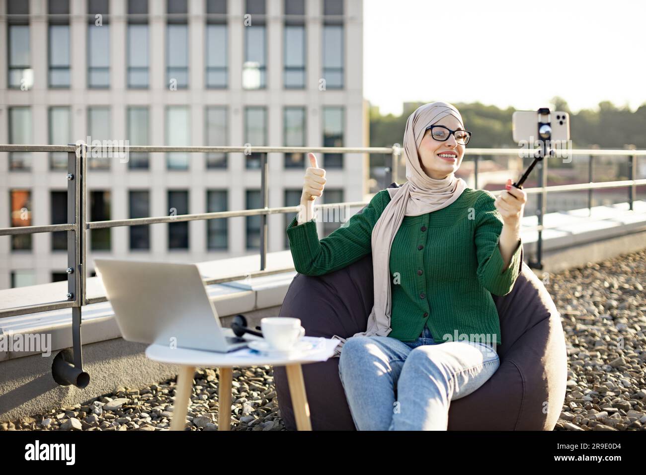 Attractive arabian woman with smartphone on selfie stick filming video content for vlog on roof ...