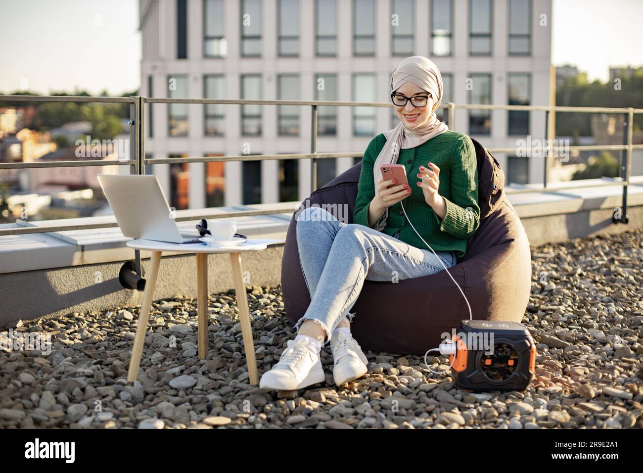Focused arabian lady in hijab holding cell phone connected to portable ...