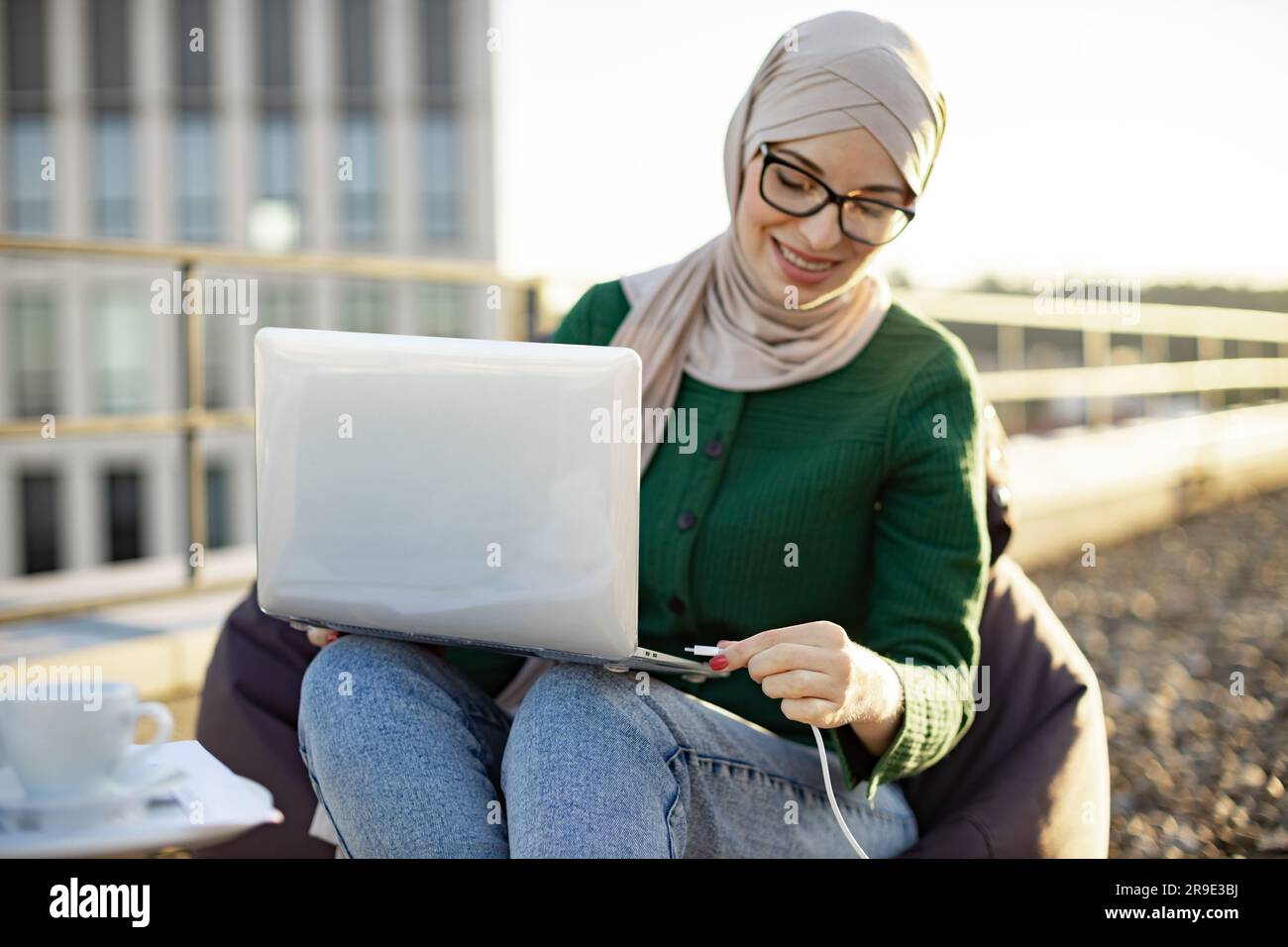 Close up view of smiling arabian woman in hijab holding laptop on knees ...