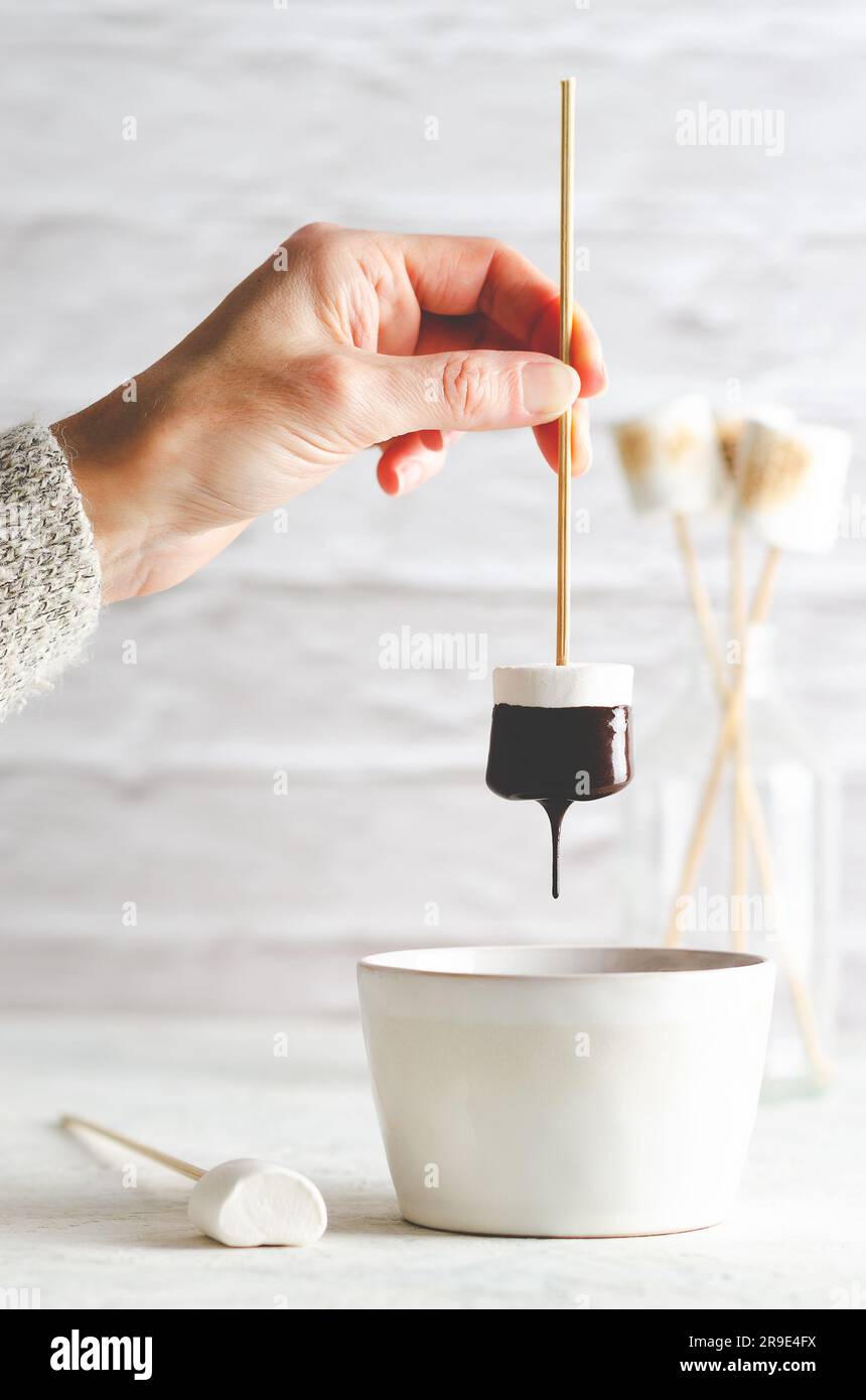 A human hand holding a white marshmallow dripping chocolate into a ...