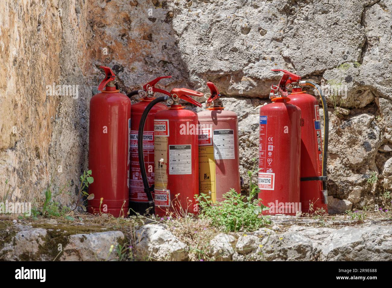 A collection of fire extinguishers standing outside against a stone ...