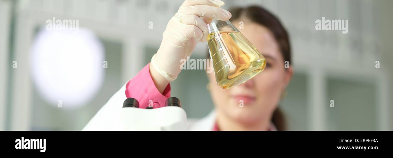 Scientist chemist looking at flask with yellow liquid or oil for ...